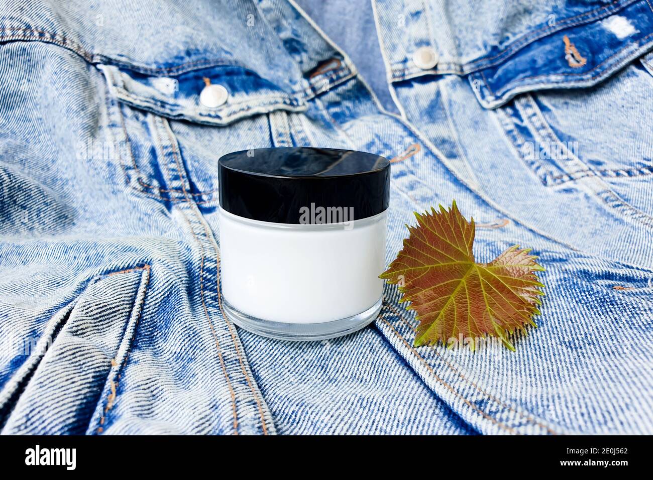 Unbranded jar of cream with a black cap and fresh leaf on denim ...