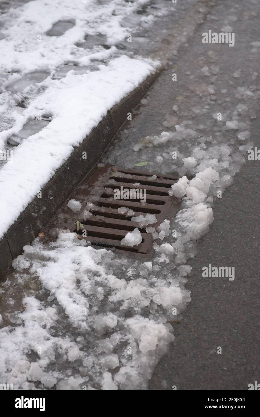 7 - Urban highway drain covered in thawing snow fall. Water runs along ...