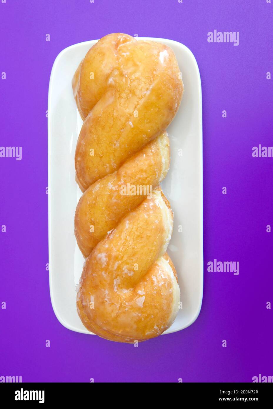 Top view flat lay of one glazed twist donut on a rectangular off white porcelain plate, on ...