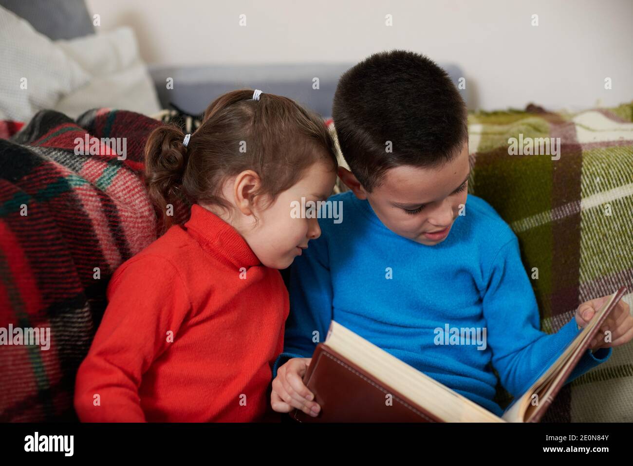 Two children sitting close to each other looking at a family photo ...