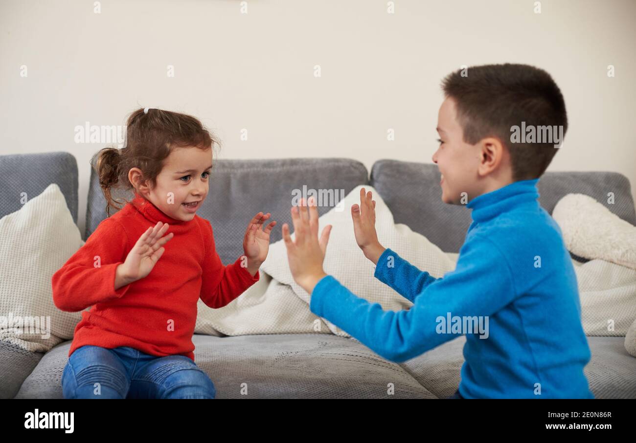 Brother and sister clap their hands sitting on the gray sofa Stock ...