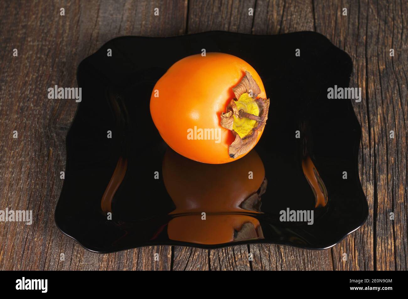 One persimmon fruit in black plate on dark wooden table Stock Photo - Alamy