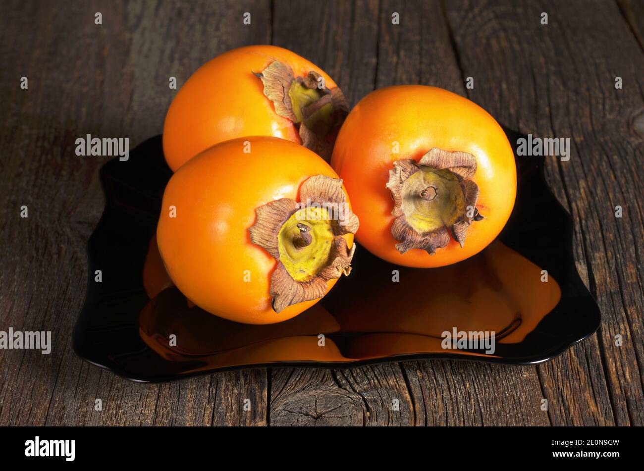Ripe persimmon fruits in black plate on dark wooden table Stock Photo ...