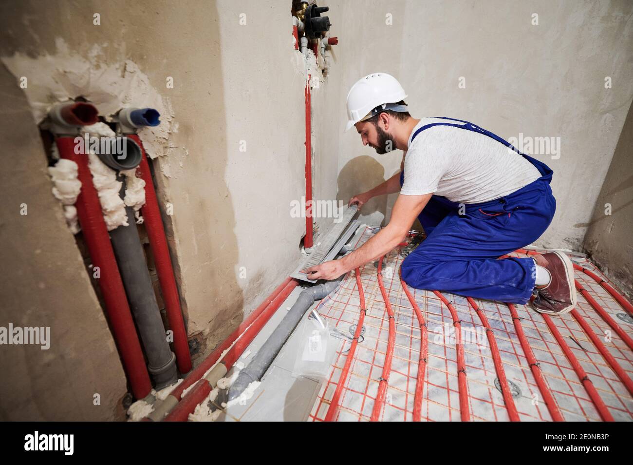 Side view of man in safety helmet installing pipes for warm floor in ...