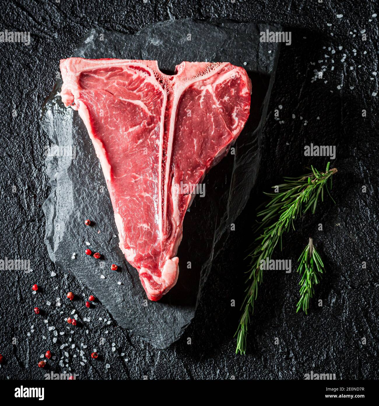 Raw and red steak with salt, pepper and rosemary on black rock Stock ...
