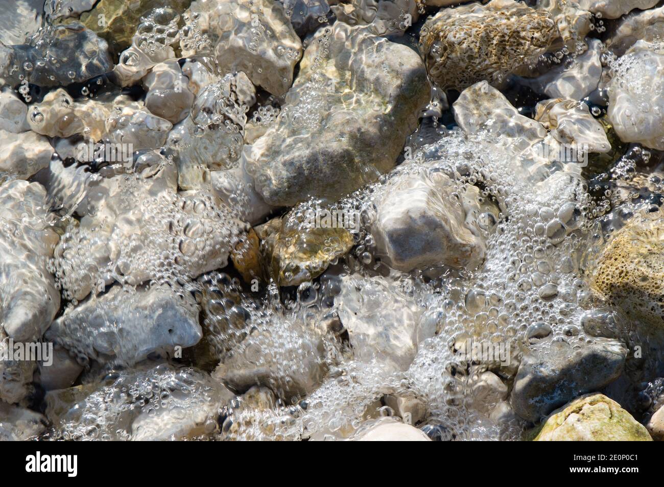 Transparent sea water and wave bubbles over beach pebbles and rocks ...