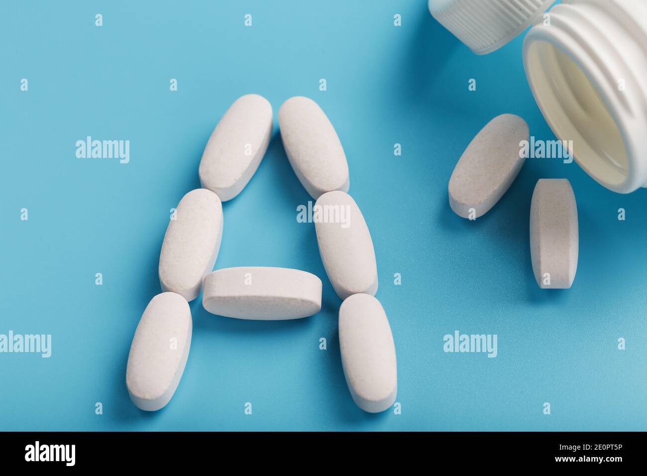 Vitamin A pills fell out of a white jar on a blue background. The ...