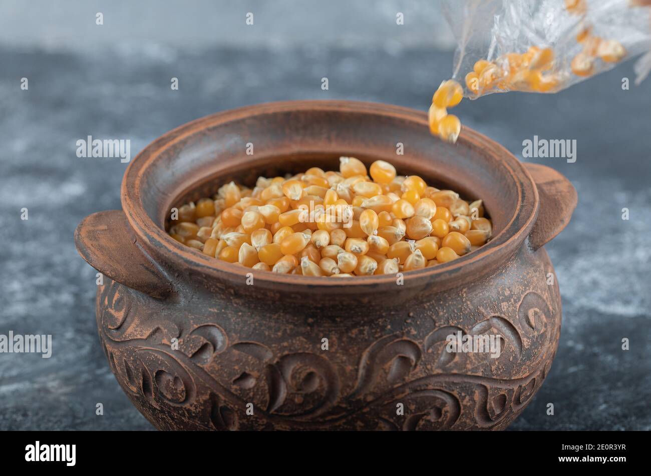 Hand filling a bowl of uncooked popcorn seeds on a marble background ...