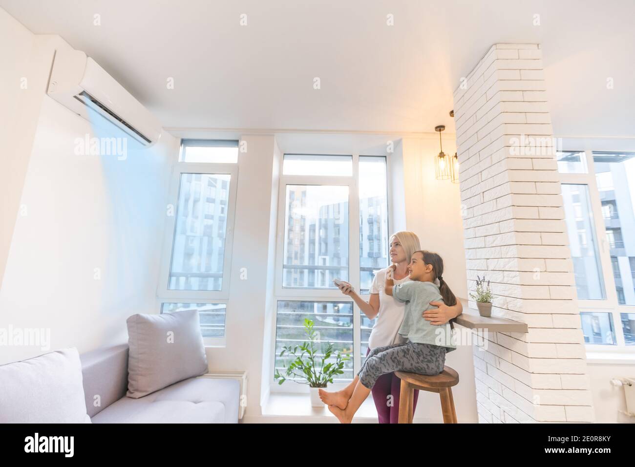 Happy family under air conditioner, mom holding remote control switch on conditioning in living ...