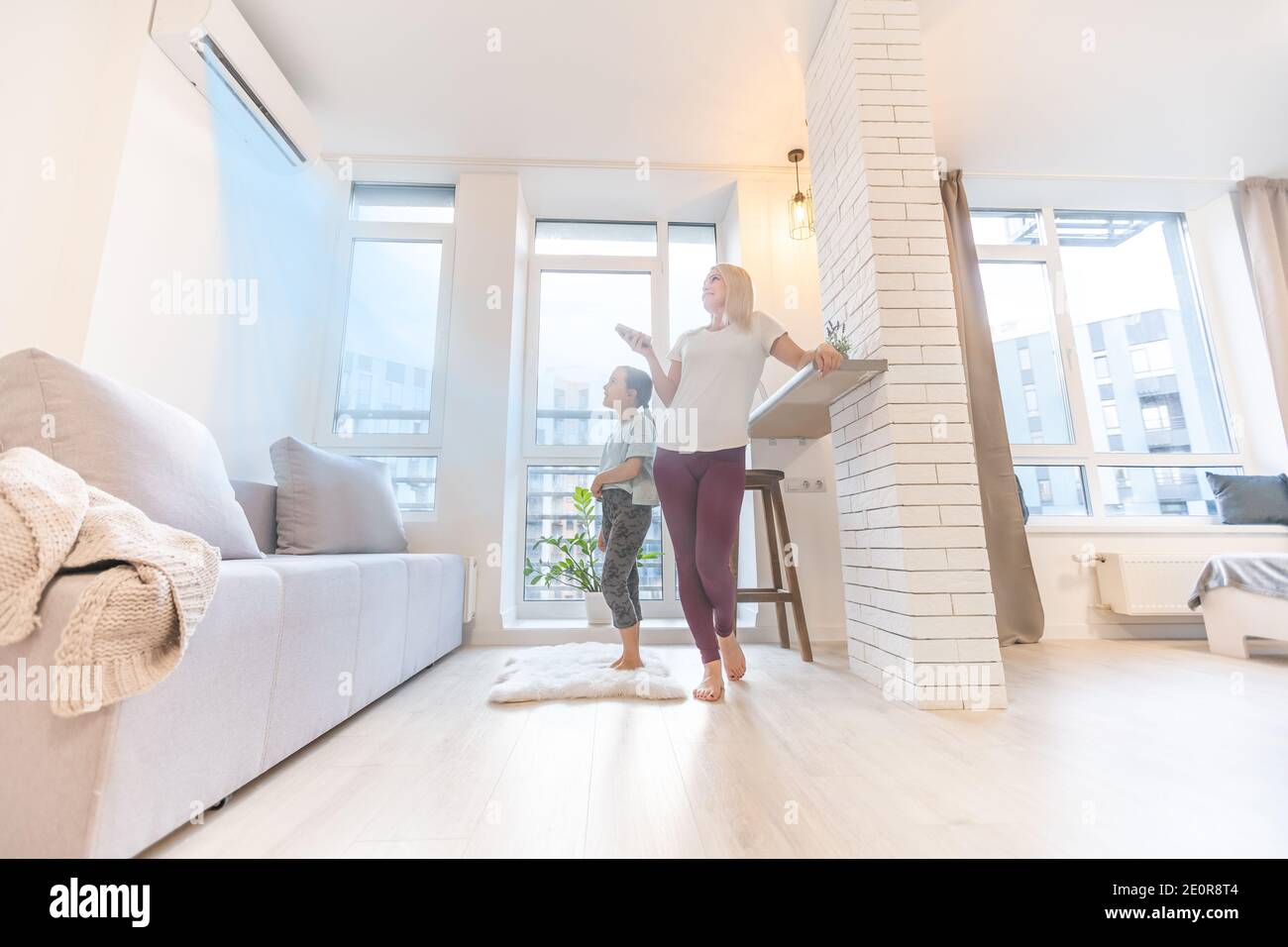 Happy family under air conditioner, mom holding remote control switch on conditioning in living ...