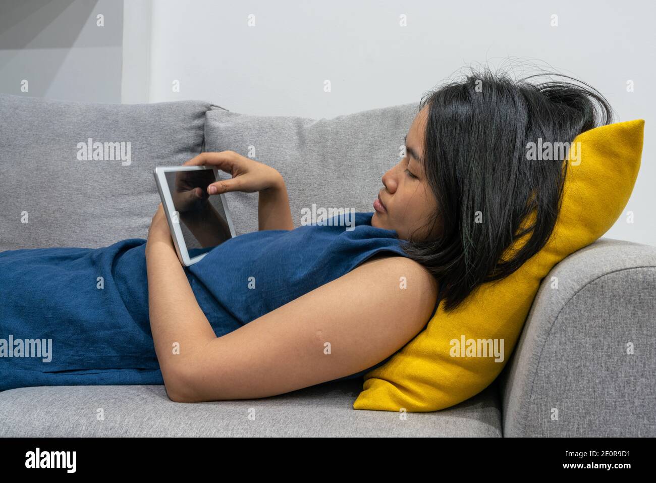 Side view of young woman lying on sofa and using tablet Stock Photo - Alamy
