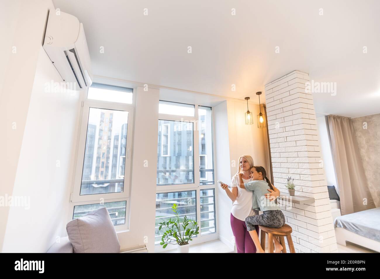 Happy family under air conditioner, mom holding remote control switch on conditioning in living ...