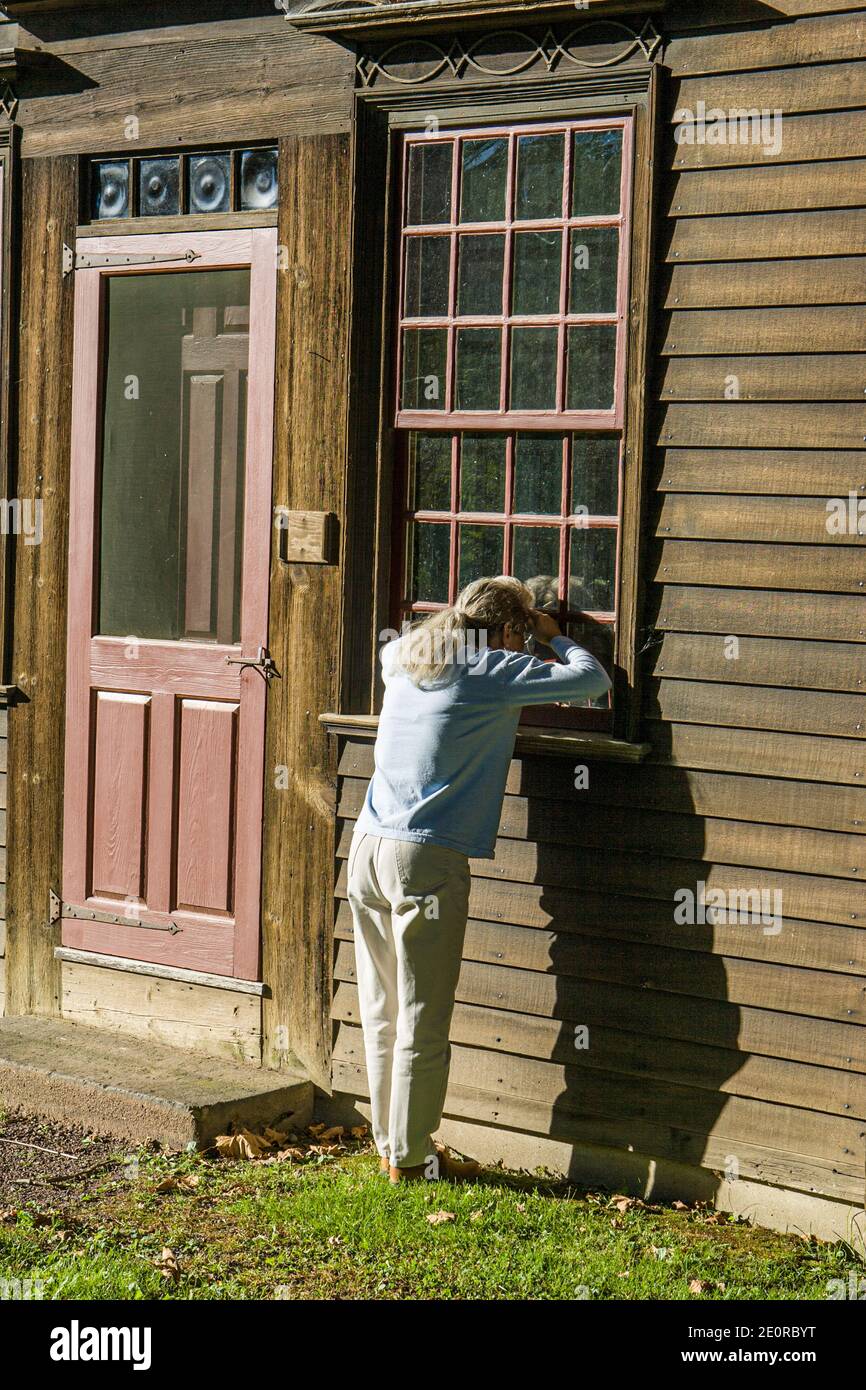 A woman peeking in one of the windows of an old home at Deerfield ...