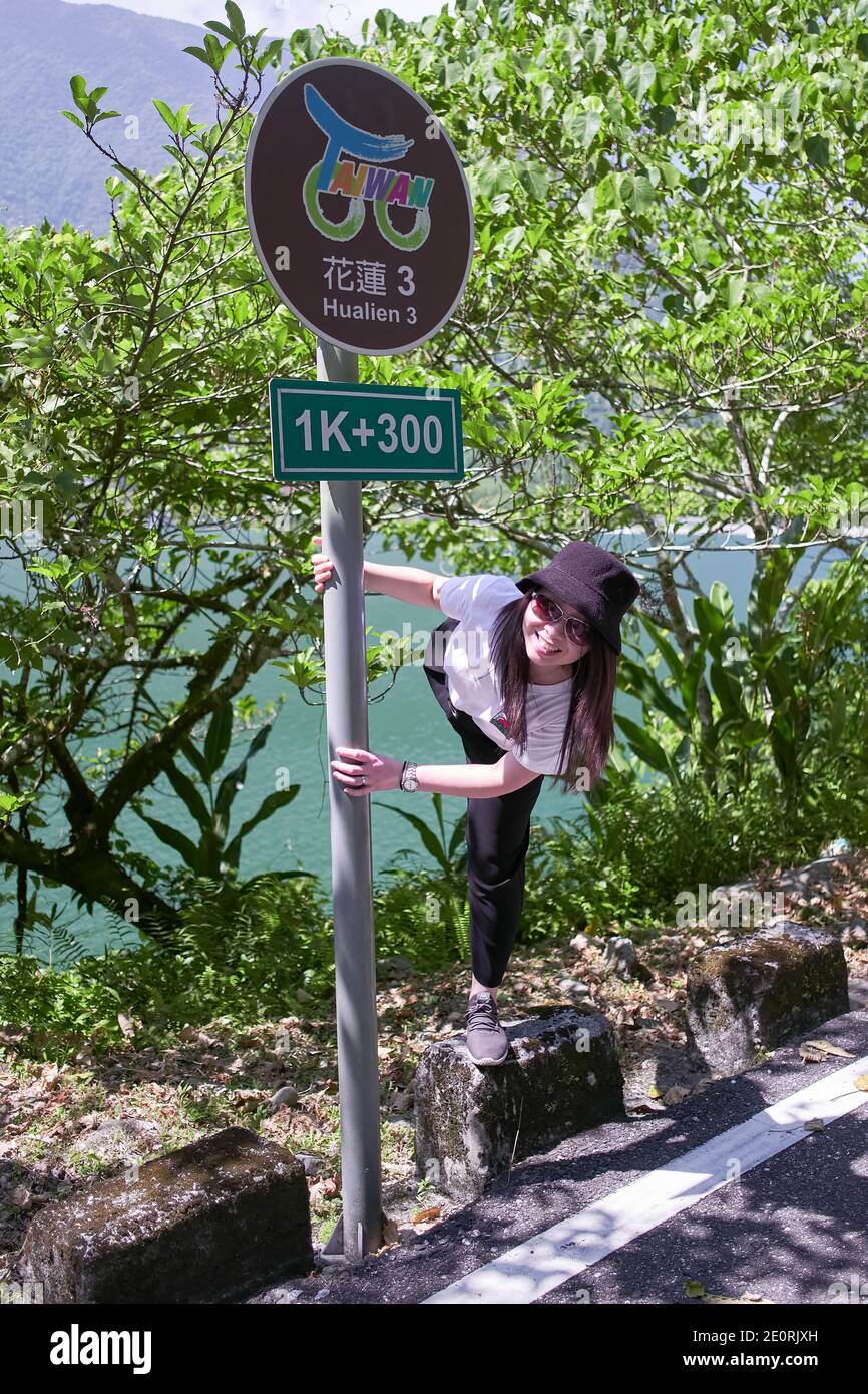 Asian woman holding onto distance marker post sign on path surrounding ...