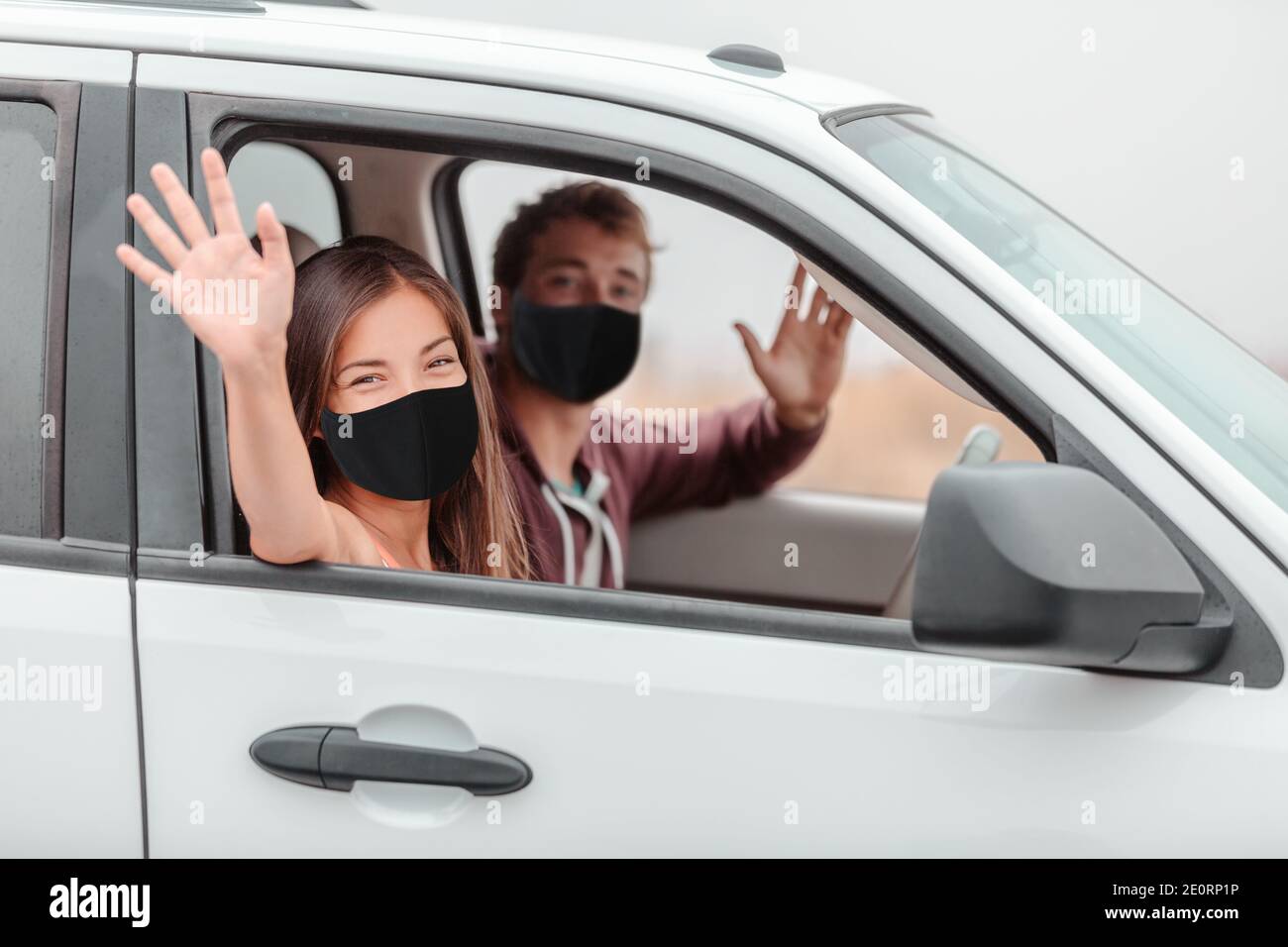 Happy driver and passenger waving hello driving new car on road trip or ...