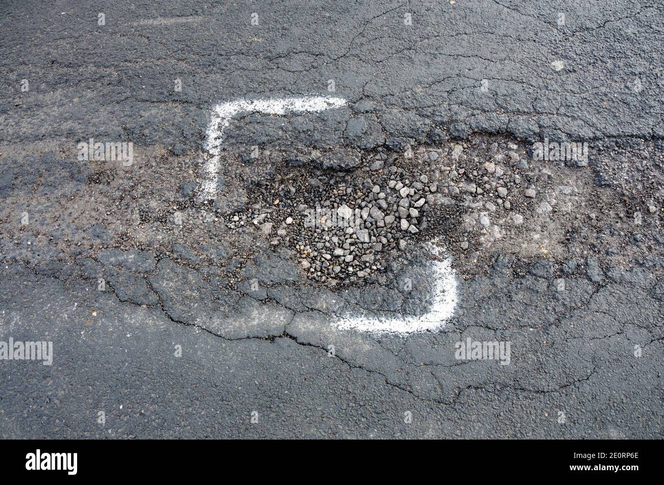 A pothole in a road in Reading, UK is marked for repair with white ...