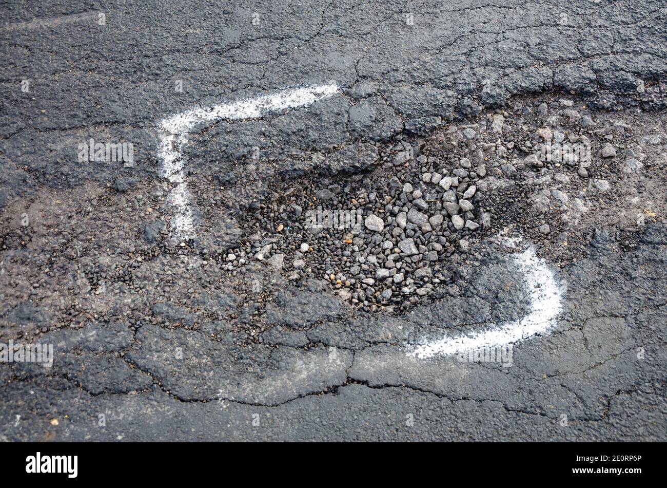 A pothole in a road in Reading, UK is marked for repair with white ...