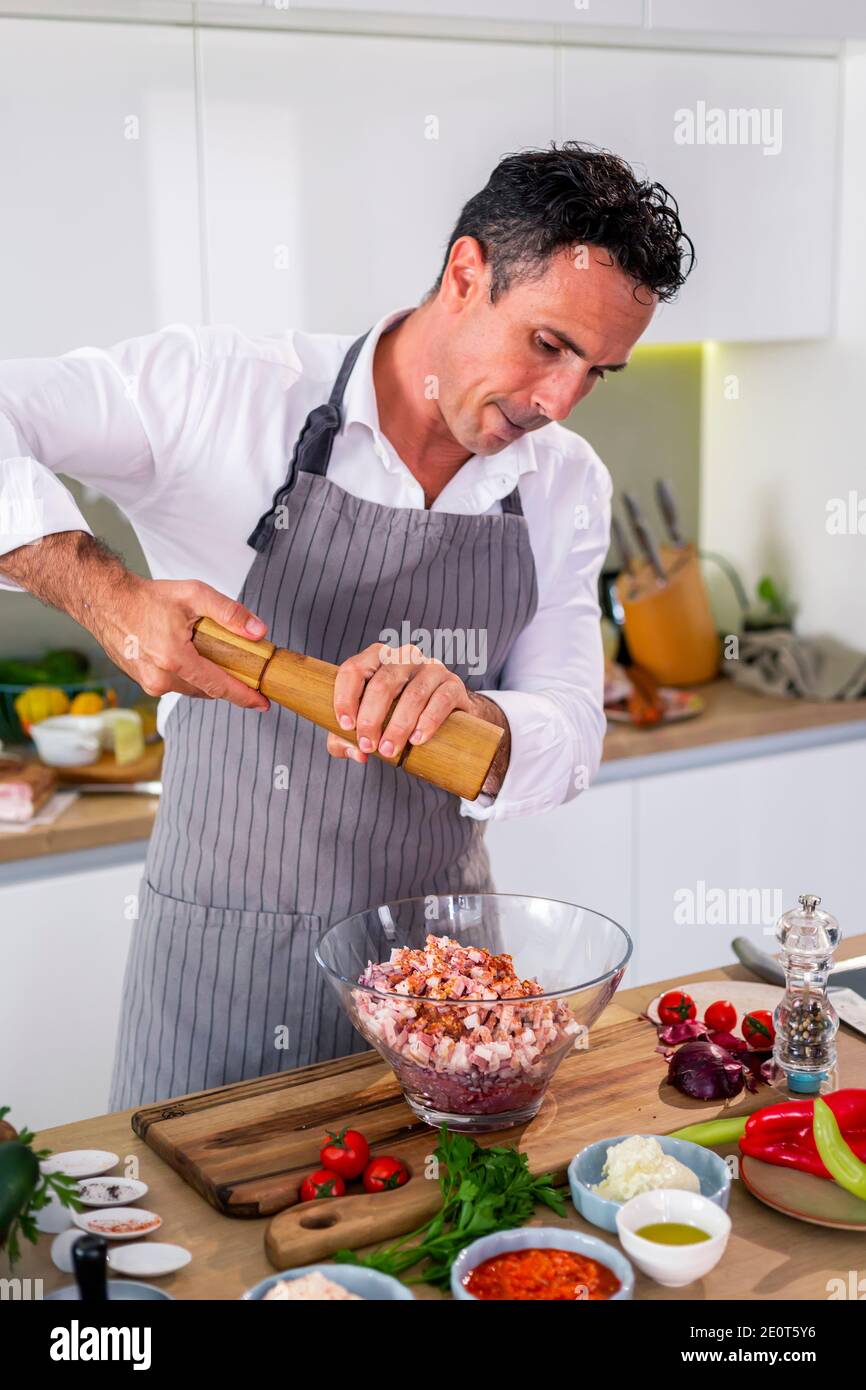 The chef adding the spices in a transparent glass bowl with meat, onion ...