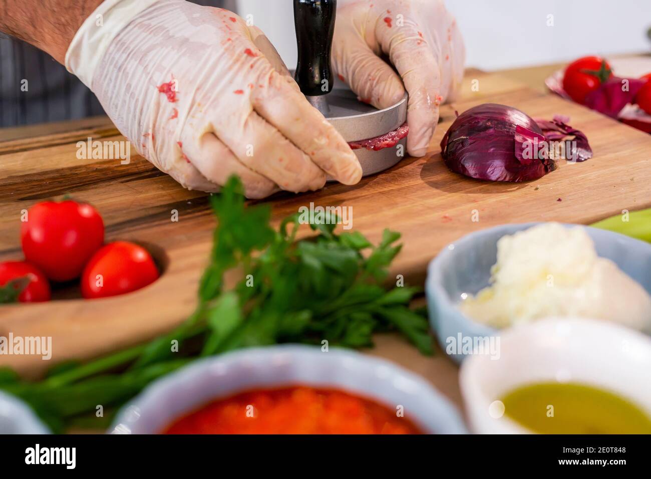 A close-up of a chef shaping meat for burgers in a press on a wooden ...