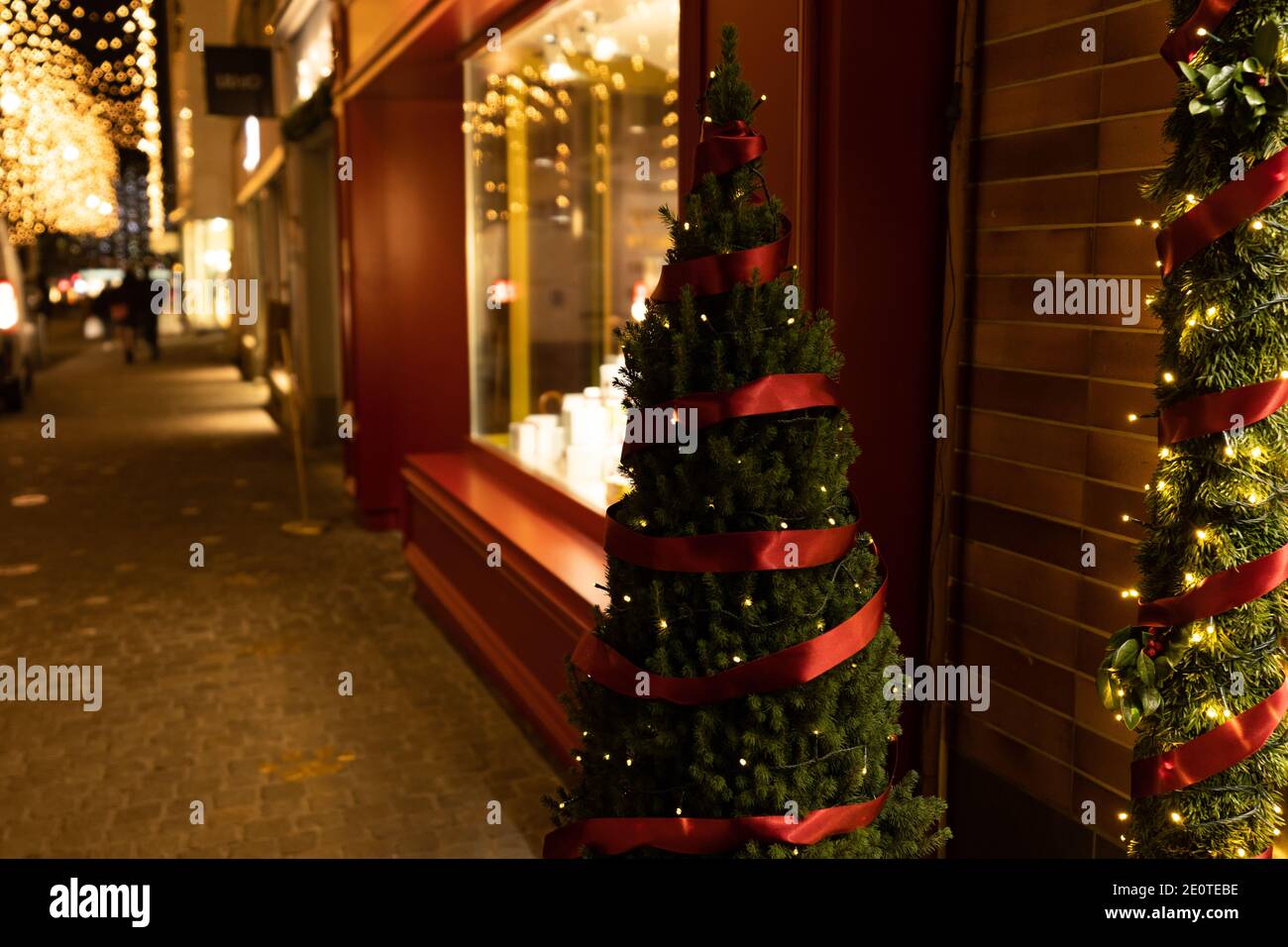 Decorated and illuminated store window with pine, red ribbon, light and ...