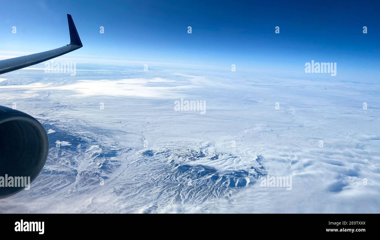 An aerial view from an airplane window of mountains, snow, clouds and ...