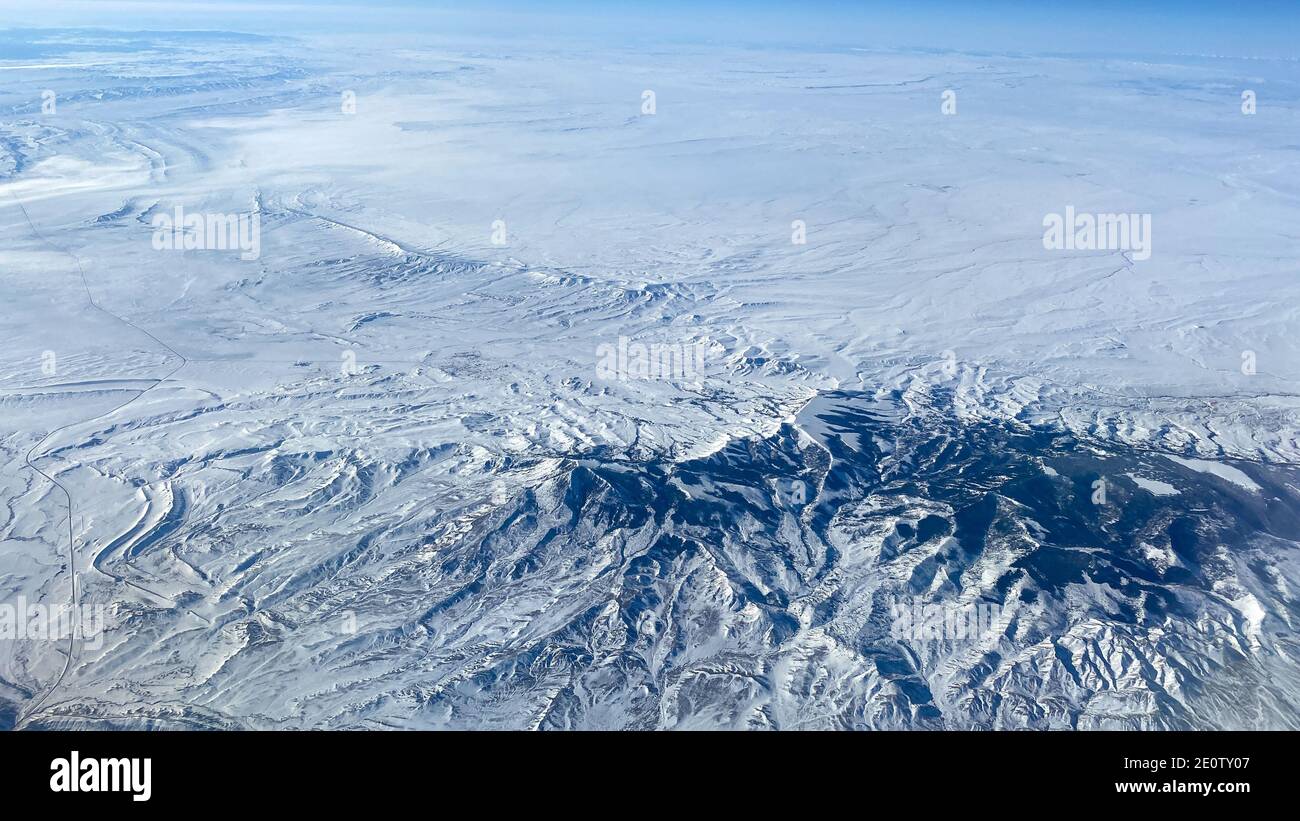 An aerial view from an airplane window of mountains, snow, clouds and ...