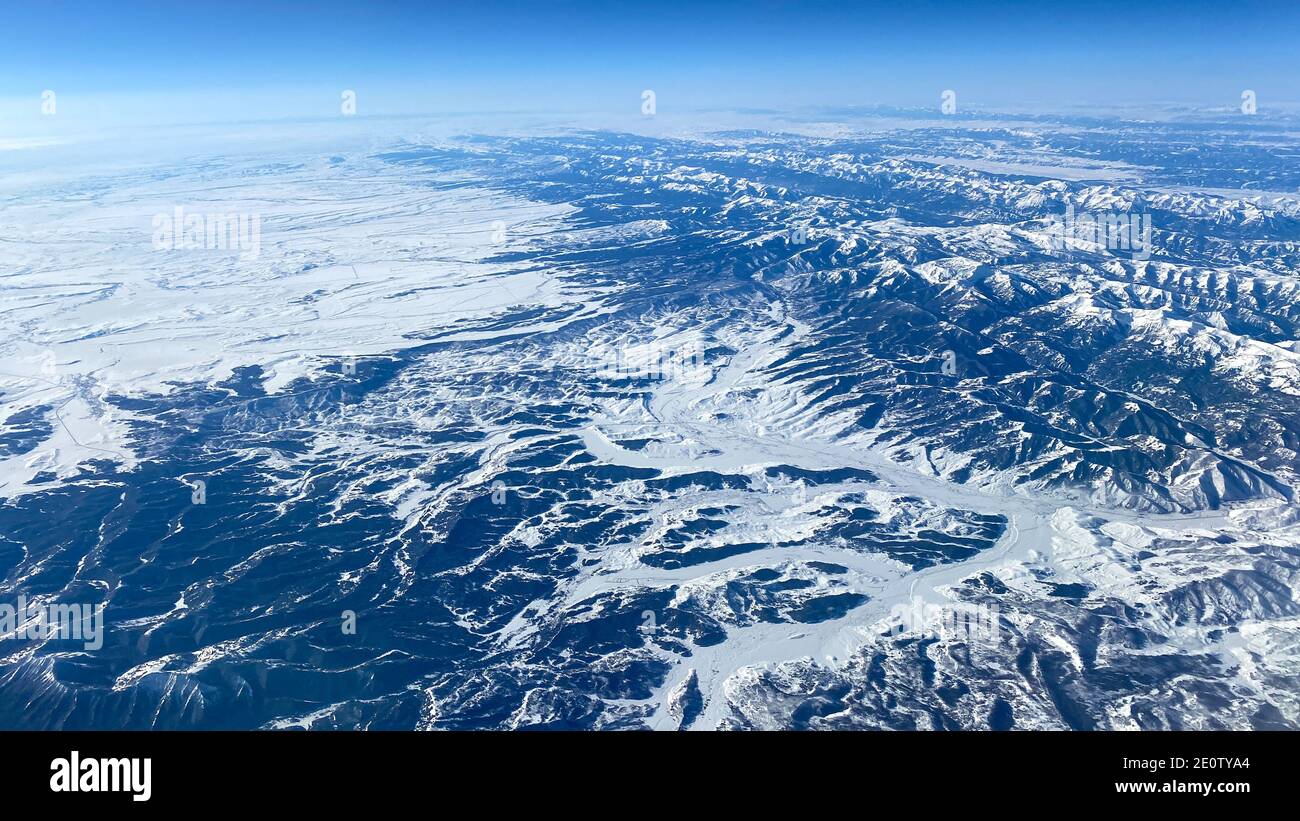An aerial view from an airplane window of mountains, snow, clouds and ...