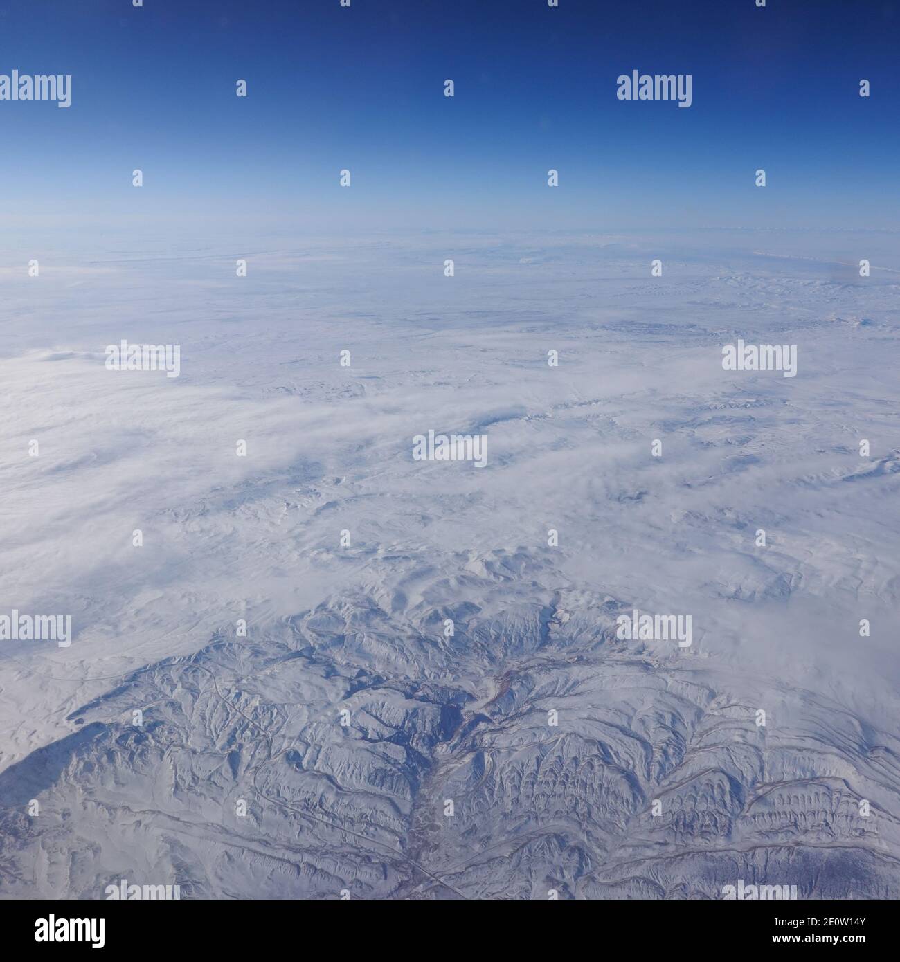 An aerial view from an airplane window of mountains, snow, clouds and ...