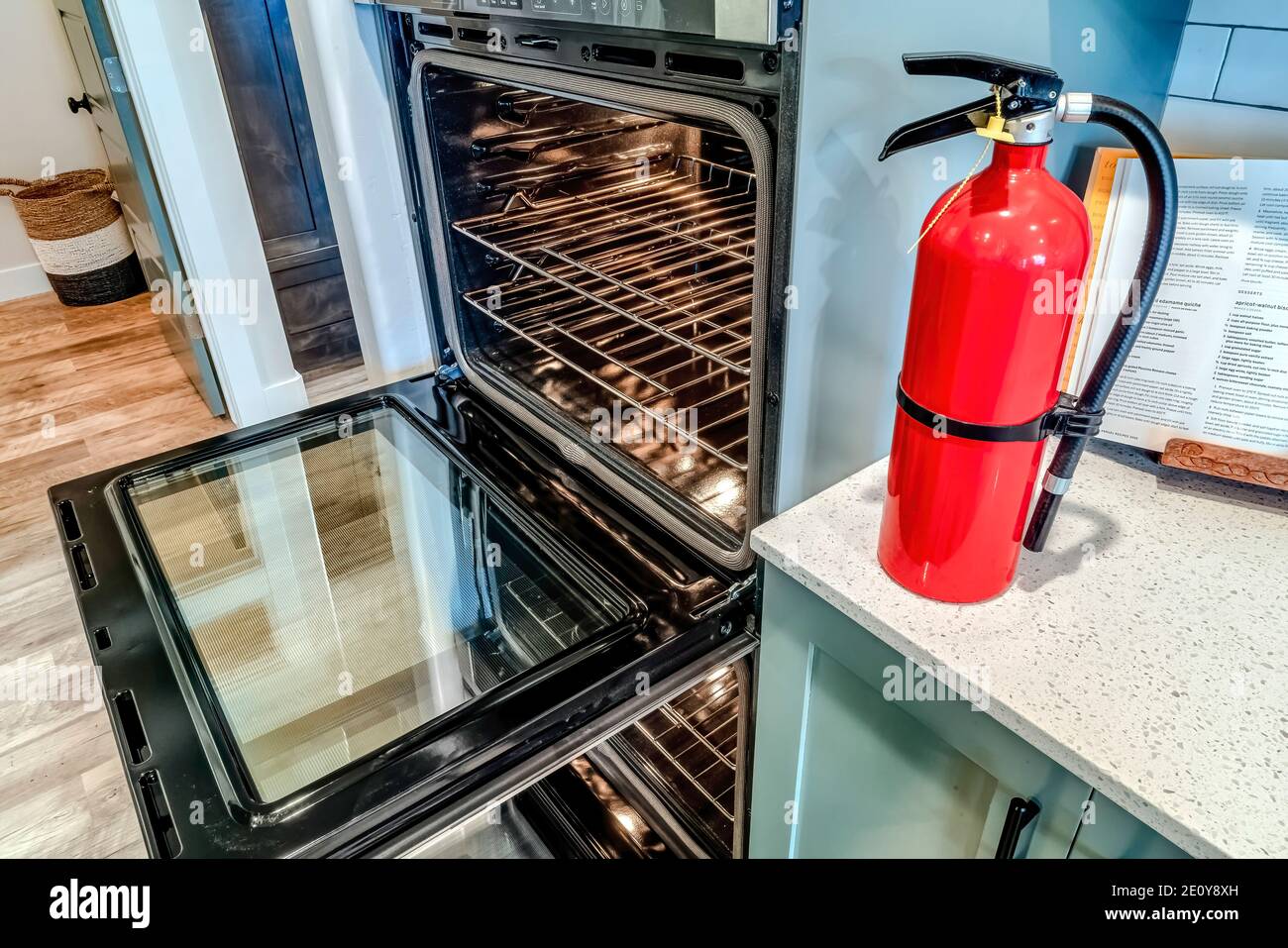 Bright red fire extinguisher and electric oven with open doors inside ...