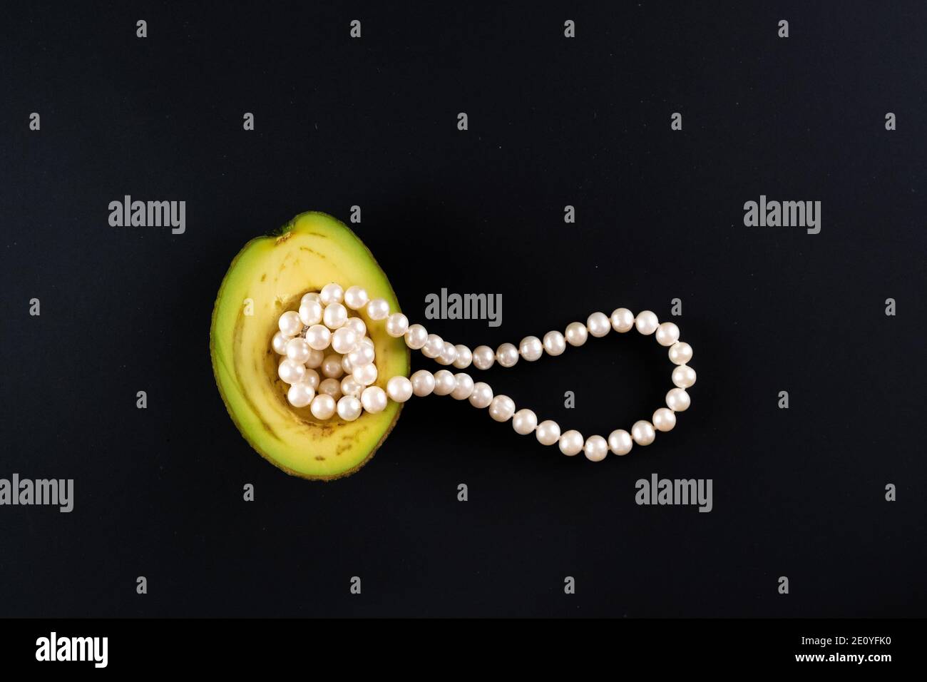 half an avocado with pearls on a black background. surrealism ...