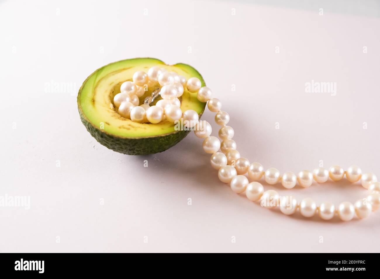 half an avocado with pearls on a light pink background. surrealism ...