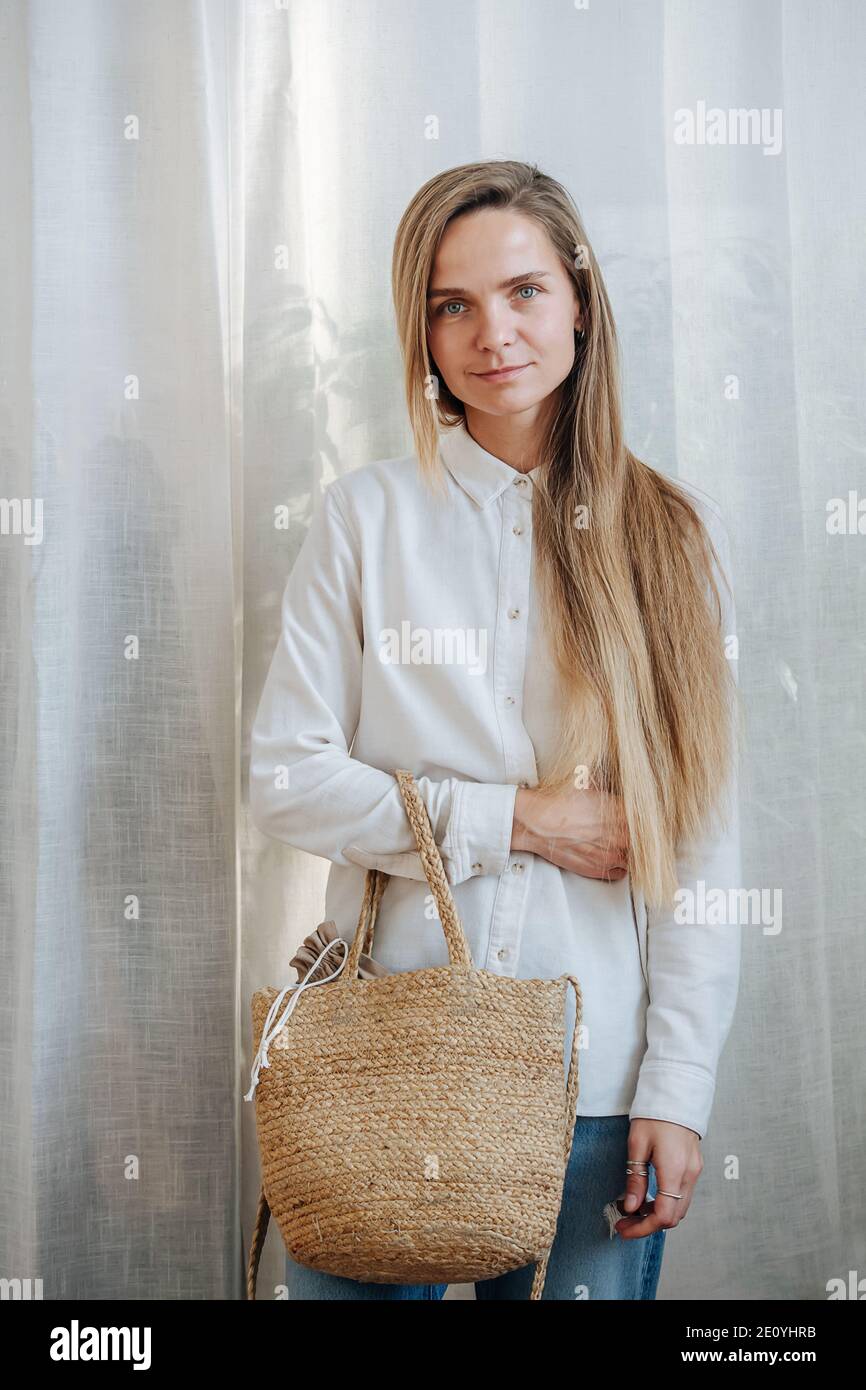 Modest woman in white sunlit room posing for a photo, holding wicker ...