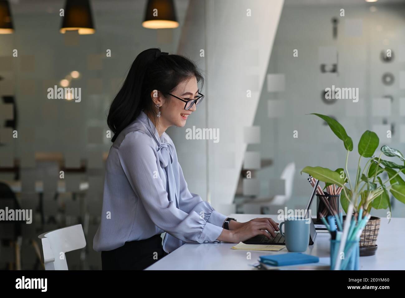 Side view of cheerful young woman sitting in front of her work desk and ...
