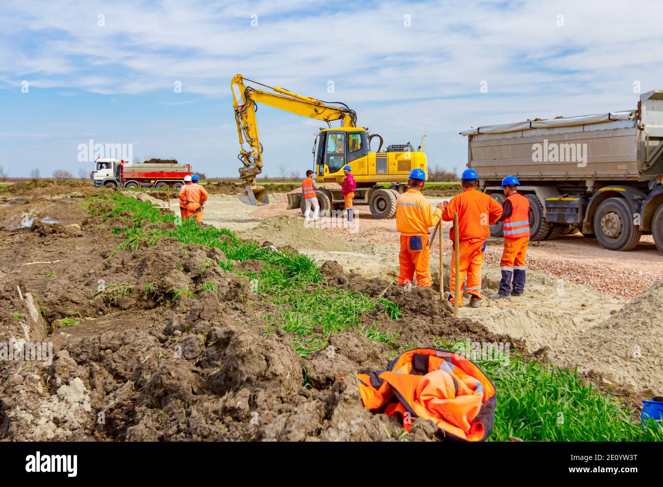 Workers are waiting for excavator to finish digging square trench on ...
