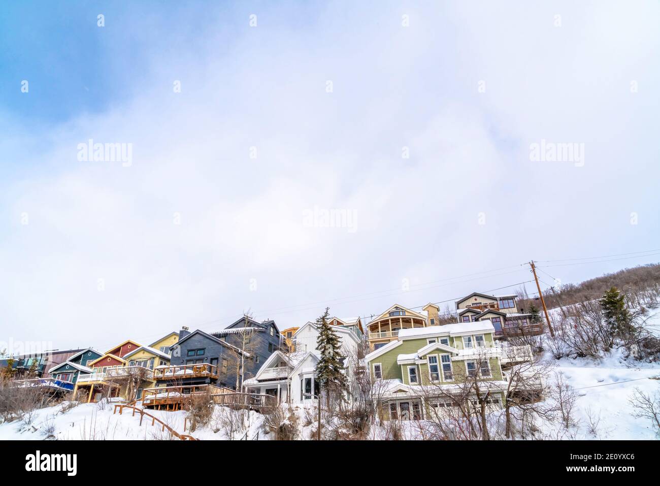 Mountain with homes on snow covered slope under skyscape of blue sky ...
