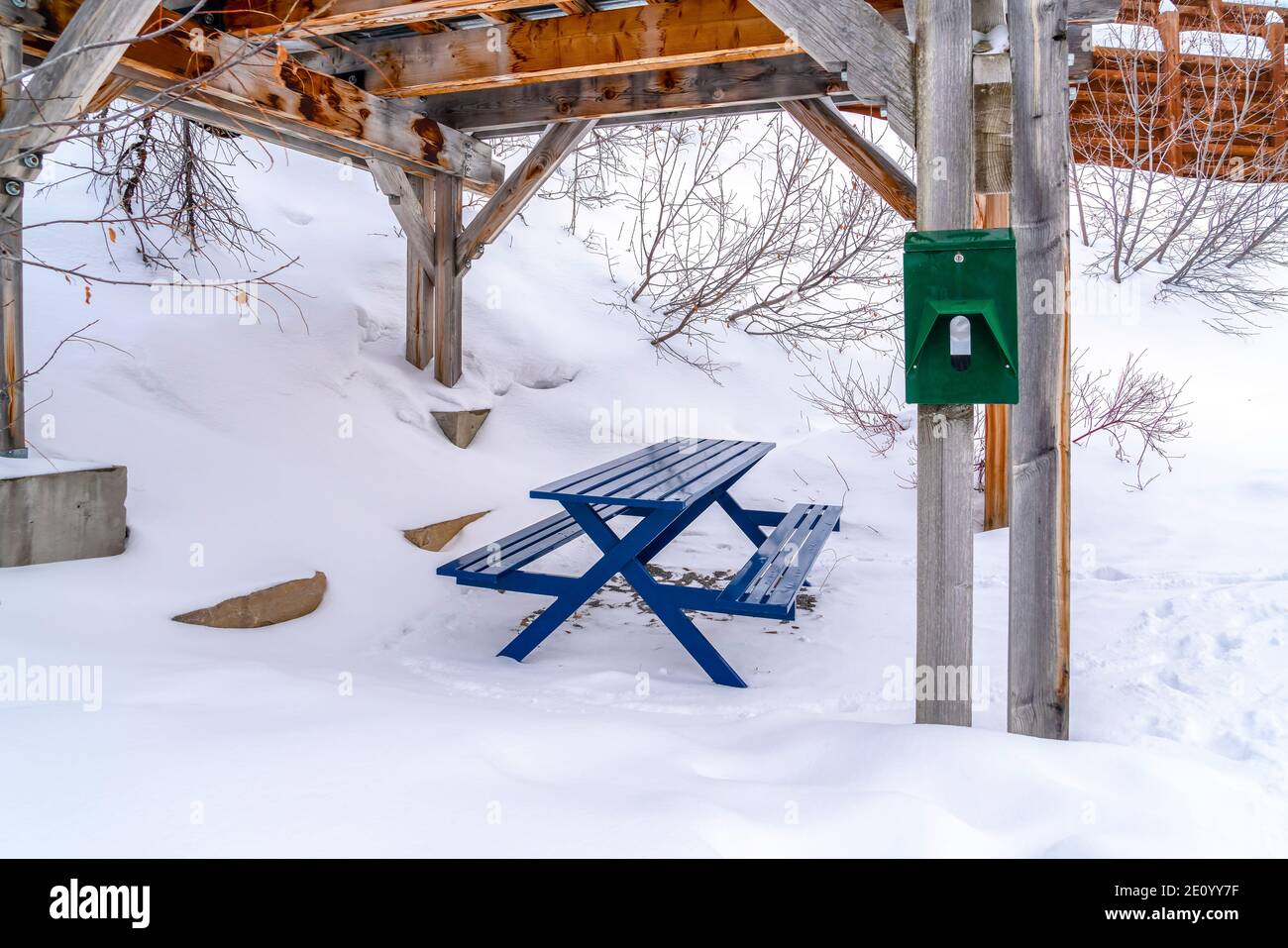 Bright blue picnic table with benches under wooden pavilion on a snowy ...