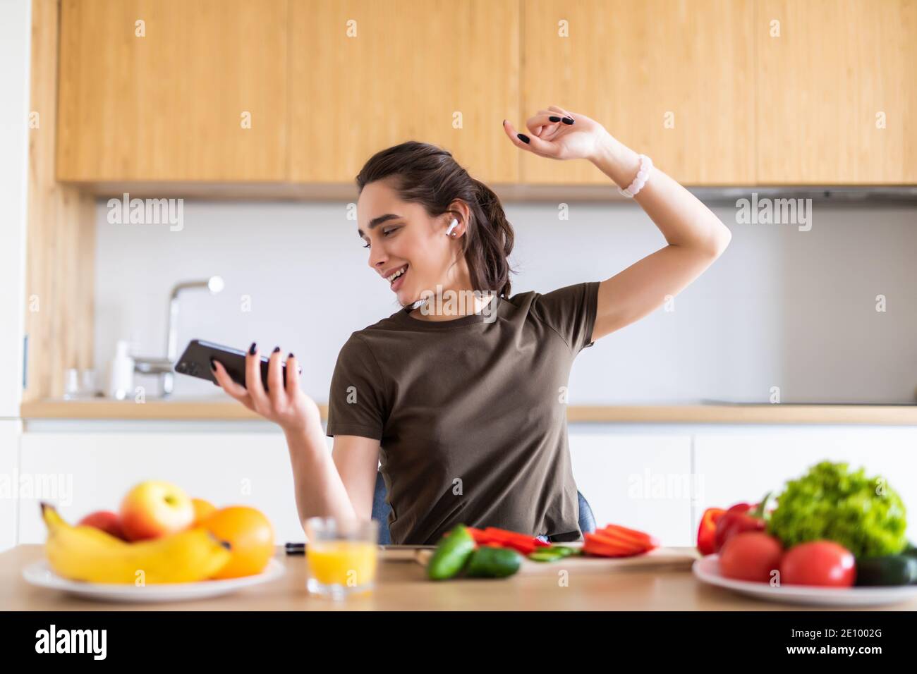 Beautiful young woman listening to music and dancing while cooking in ...