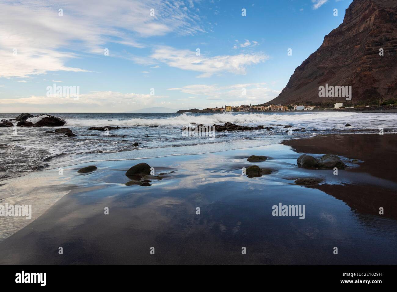 Sandy beach beach with stones, reflection from the sky, behind village ...