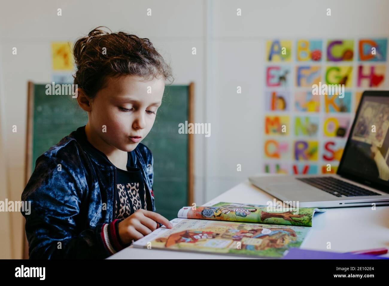 Little girl learning with reading book and laptop, homeschooling Stock ...