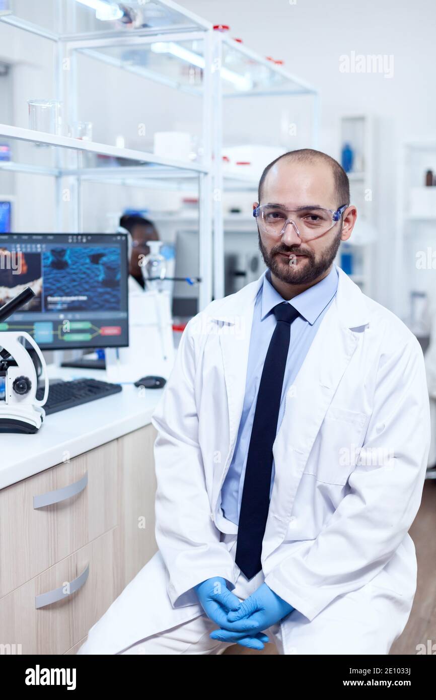 Healthcare researcher wearing lab coat and protective glasses looking ...
