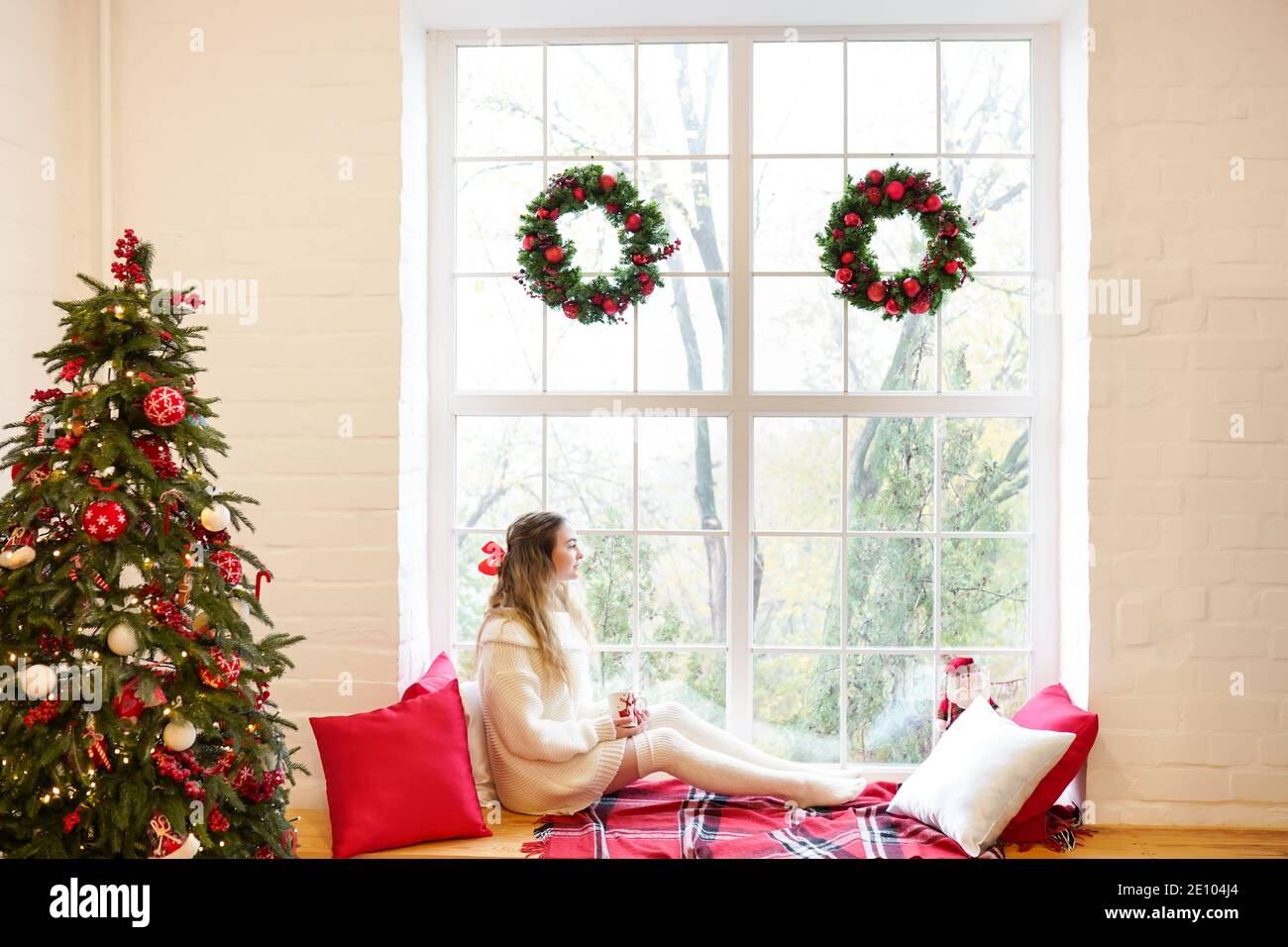 Young beautiful woman sitting home by the window wearing knitted warm ...