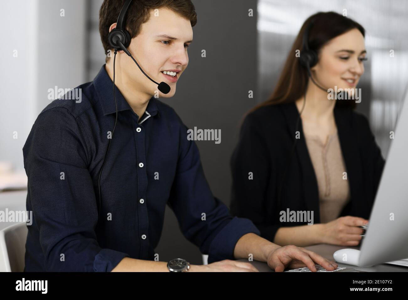 Two young people in headsets are talking to the clients, while sitting ...