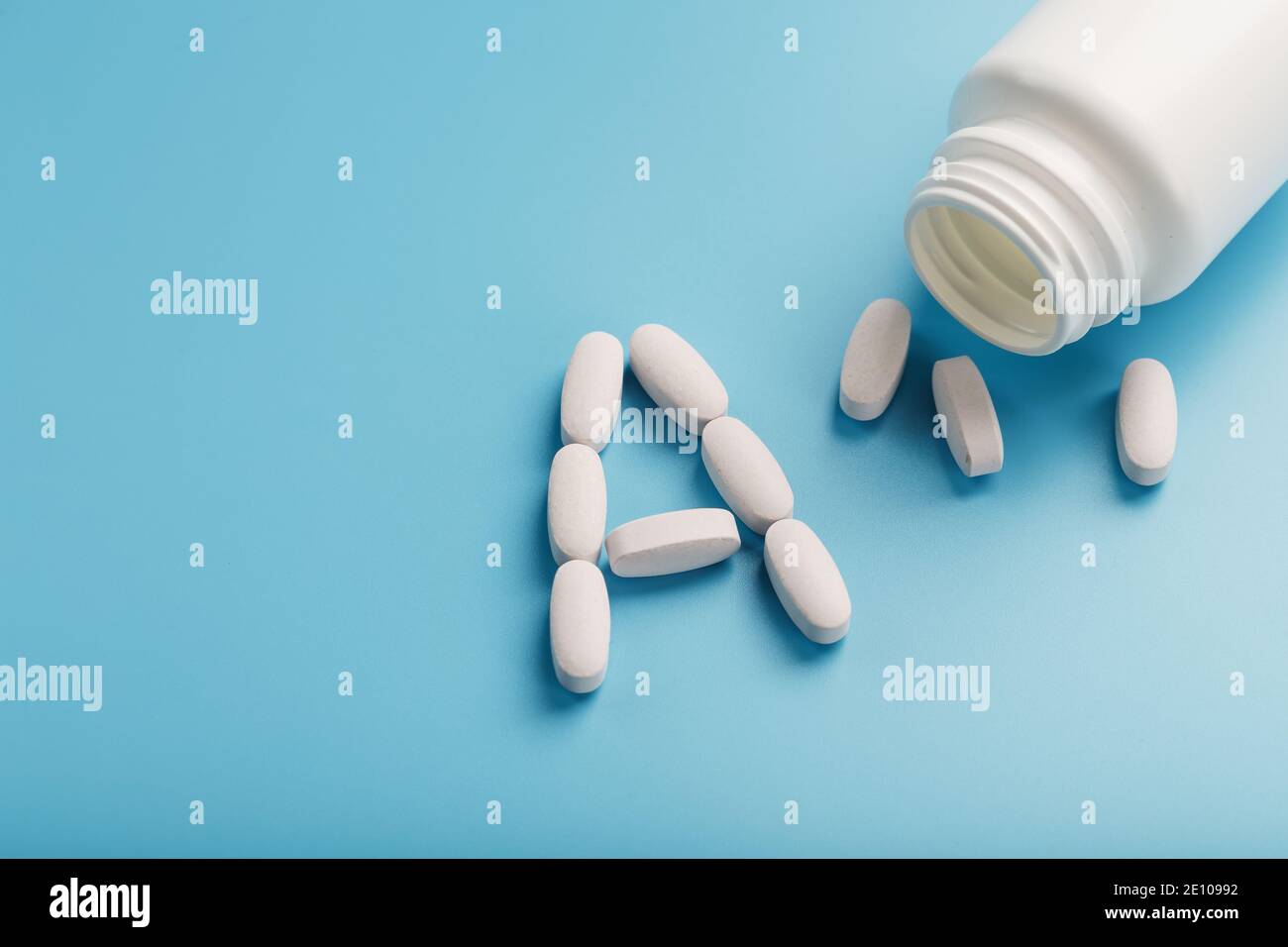 Vitamin A pills fell out of a white jar on a blue background. The ...