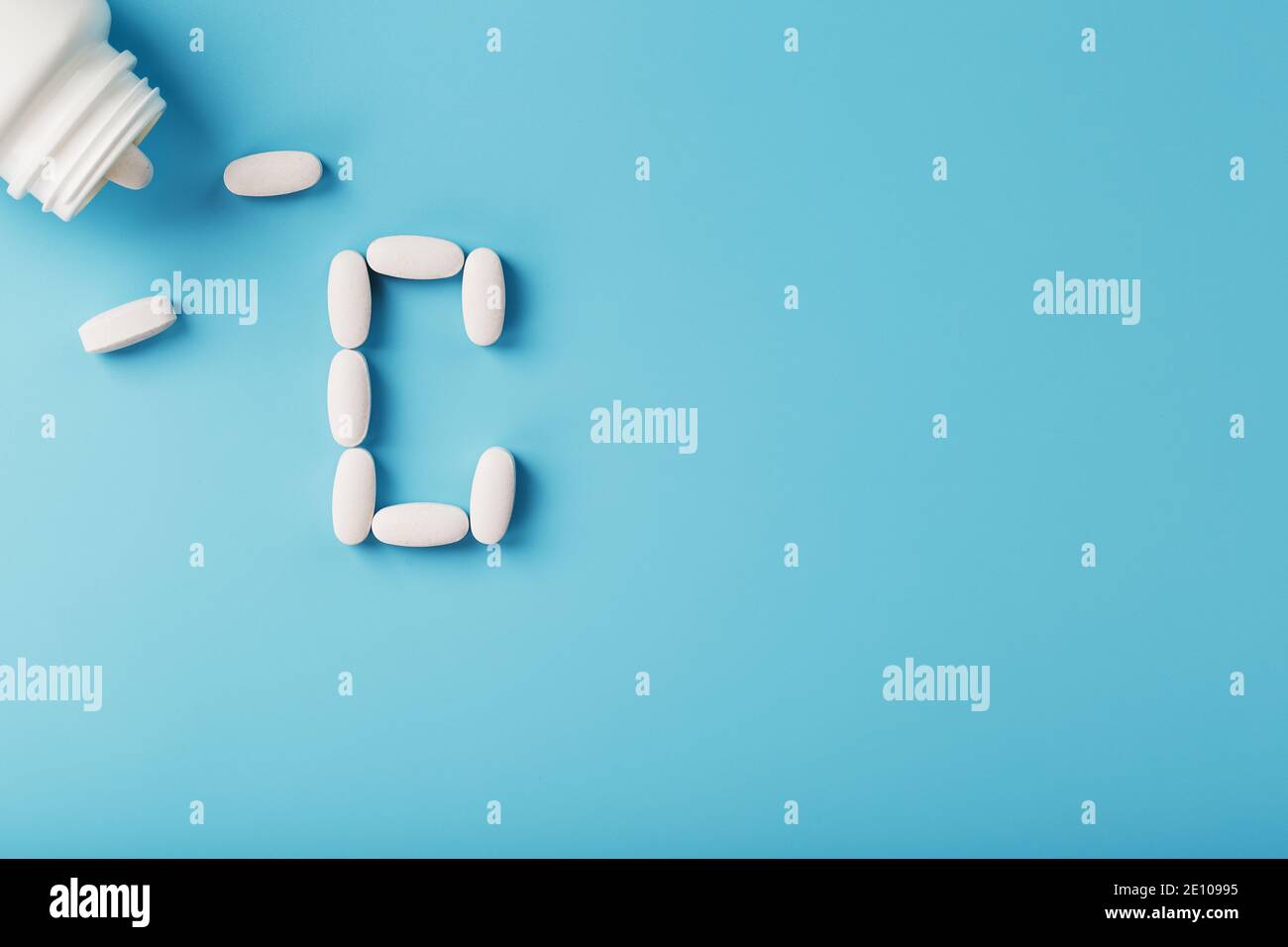The letter of vitamin C in capsules pour out from the jar on a blue ...
