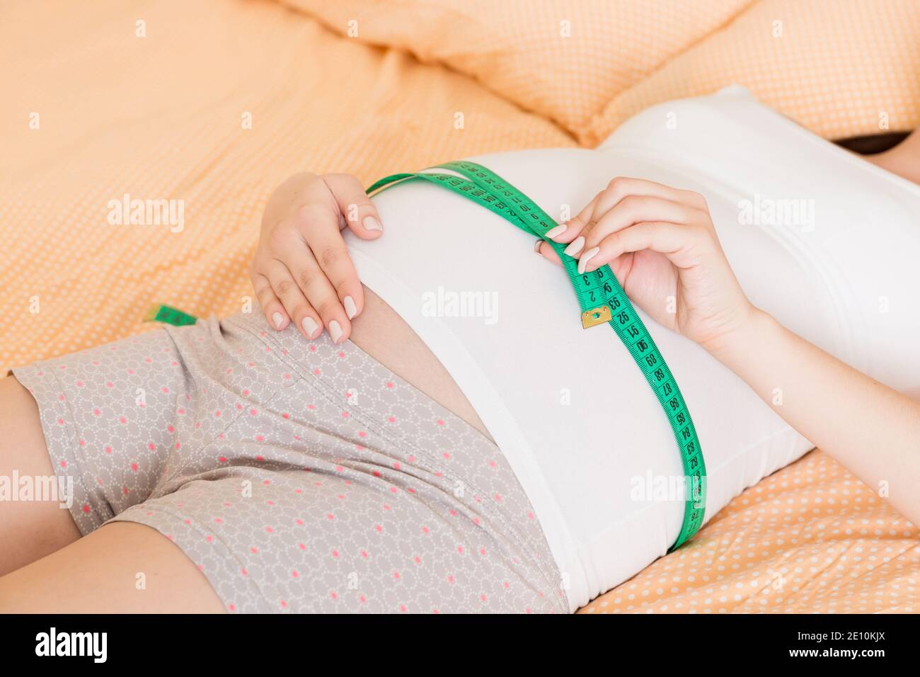 Young beautiful pregnant girl measuring her belly with a tape in home ...