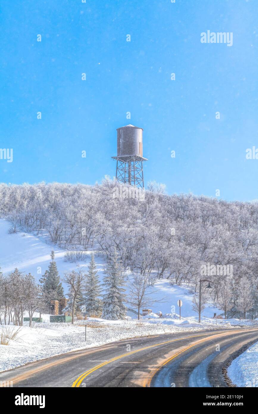 Road along hill slope with trees and water tank on a snowy setting in ...