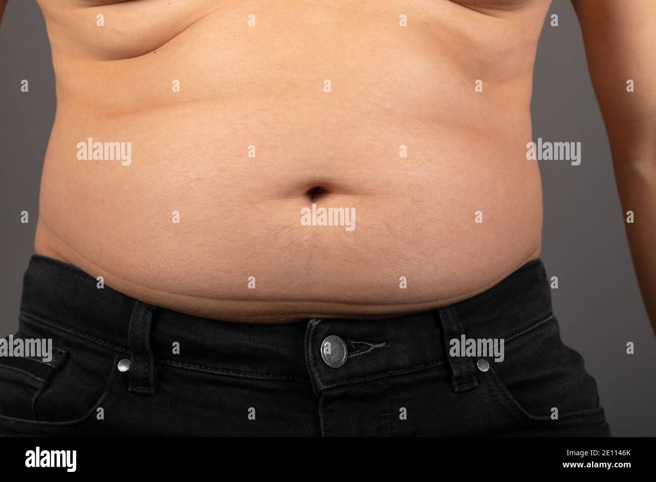 Close up picture of young man's bloated stomach in front of grey ...