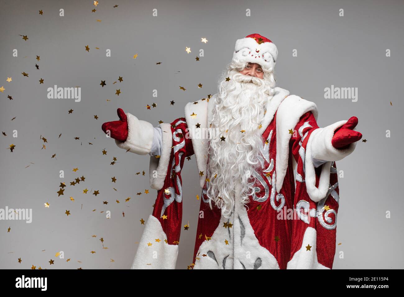 Santa Claus under golden stars confetti makes welcome gesture on gray ...