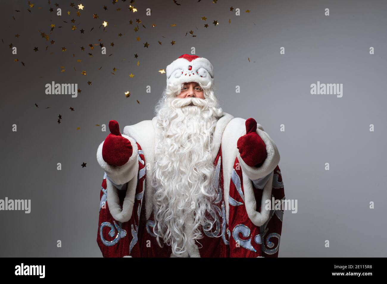 Santa Claus under golden confetti posing with thumbs up on gray studio ...