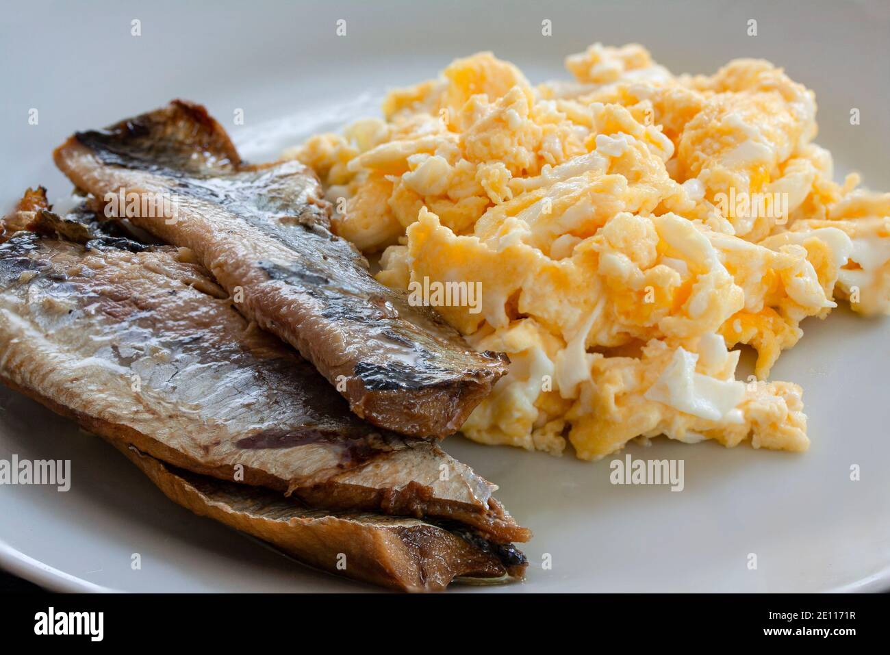 Kippers with scrambled eggs served on a white plate. A kipper is a ...